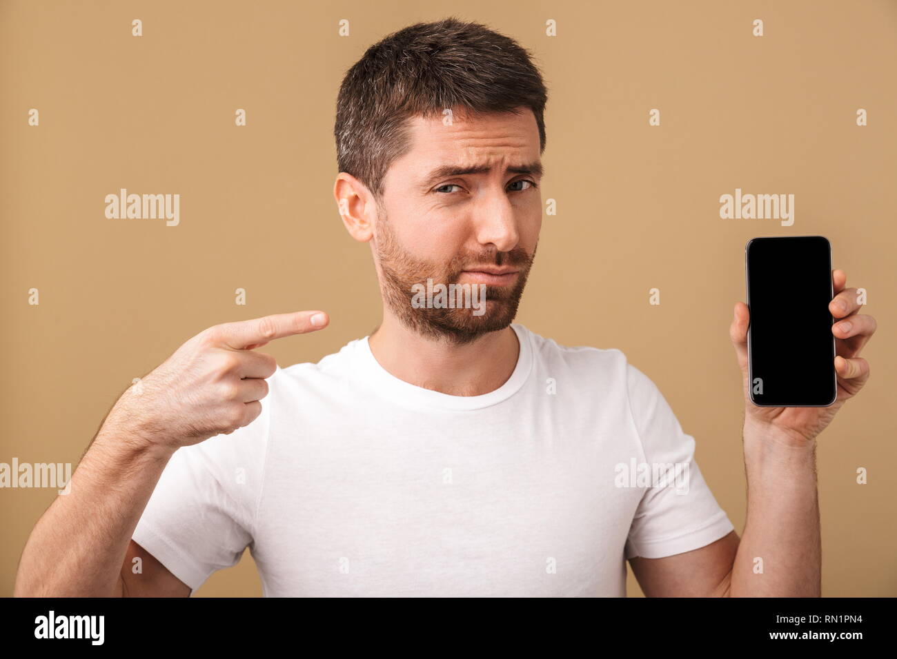 Confused young casual man showing blank screen mobile phone isolated ...