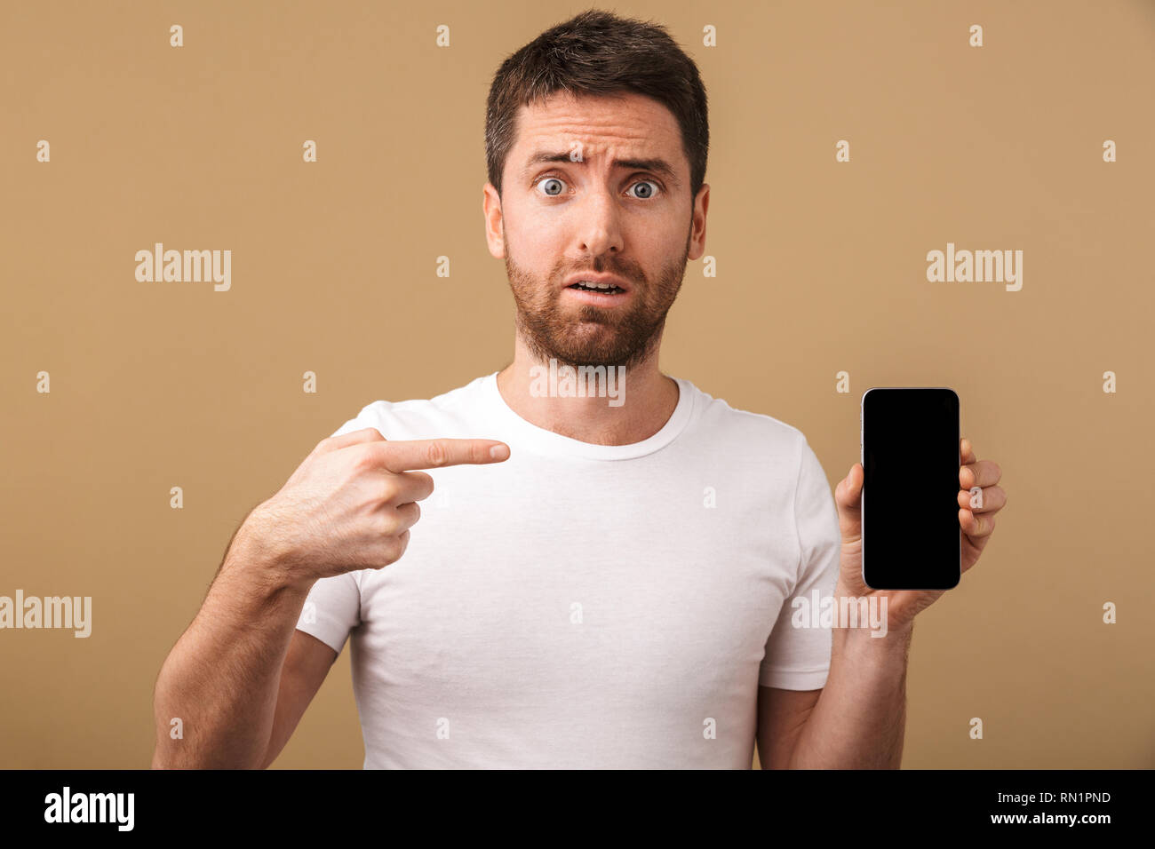 Confused young casual man showing blank screen mobile phone isolated ...
