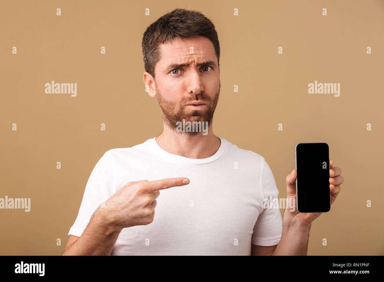 Confused young casual man showing blank screen mobile phone isolated ...