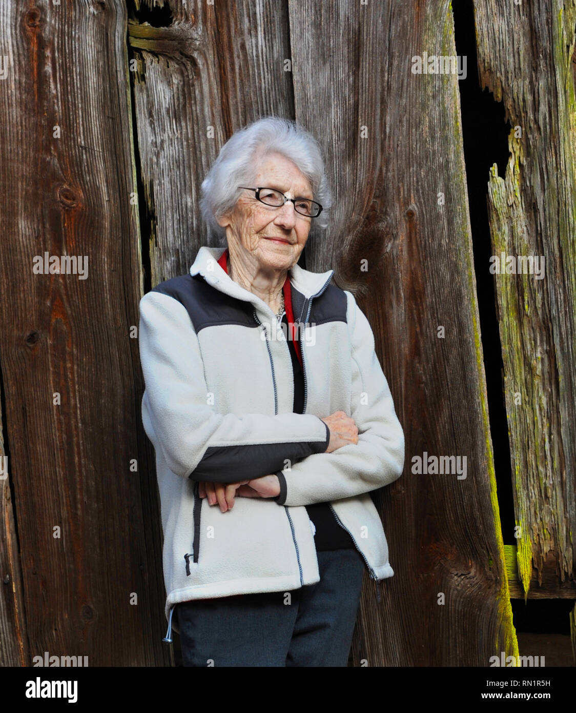Elderly woman leans against an old wooden barn. Her face is serene as ...