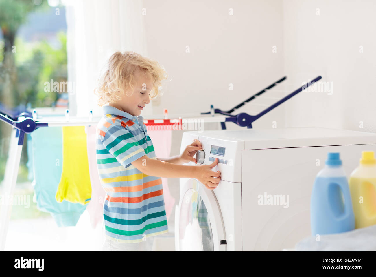 Child in laundry room with washing machine or tumble dryer. Kid helping ...