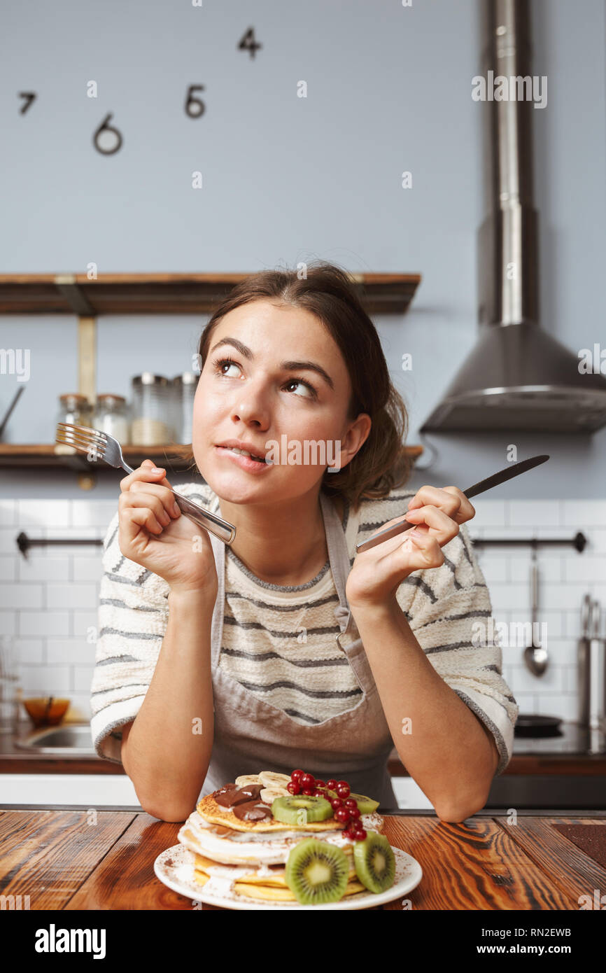 Image of a thinking beautiful young woman in kitchen cooking and eat ...