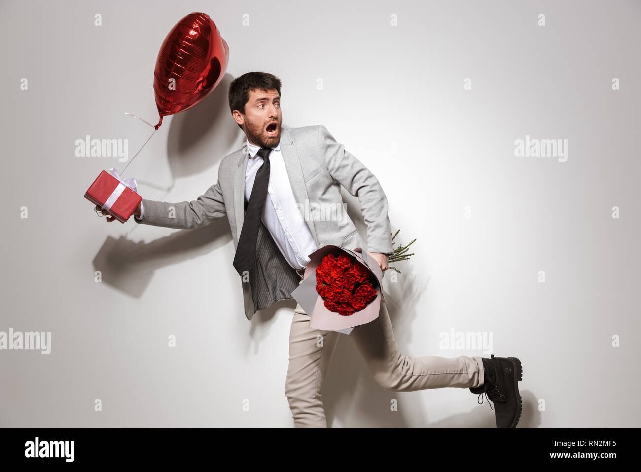 Portrait of a handsome confused young man wearing suit running isolated ...