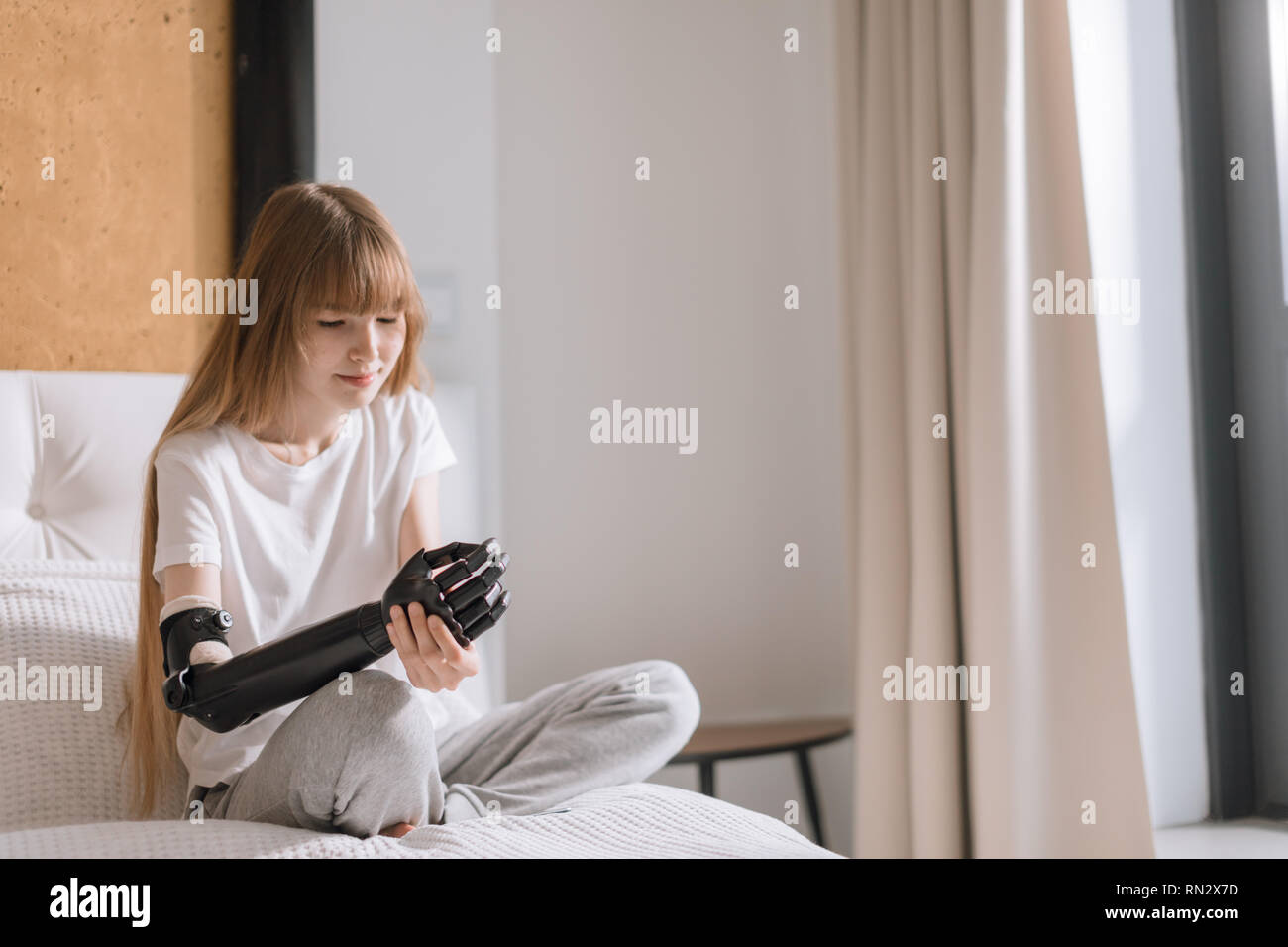 beautiful girl looking at her prosthetic arm while sitting on the bed ...
