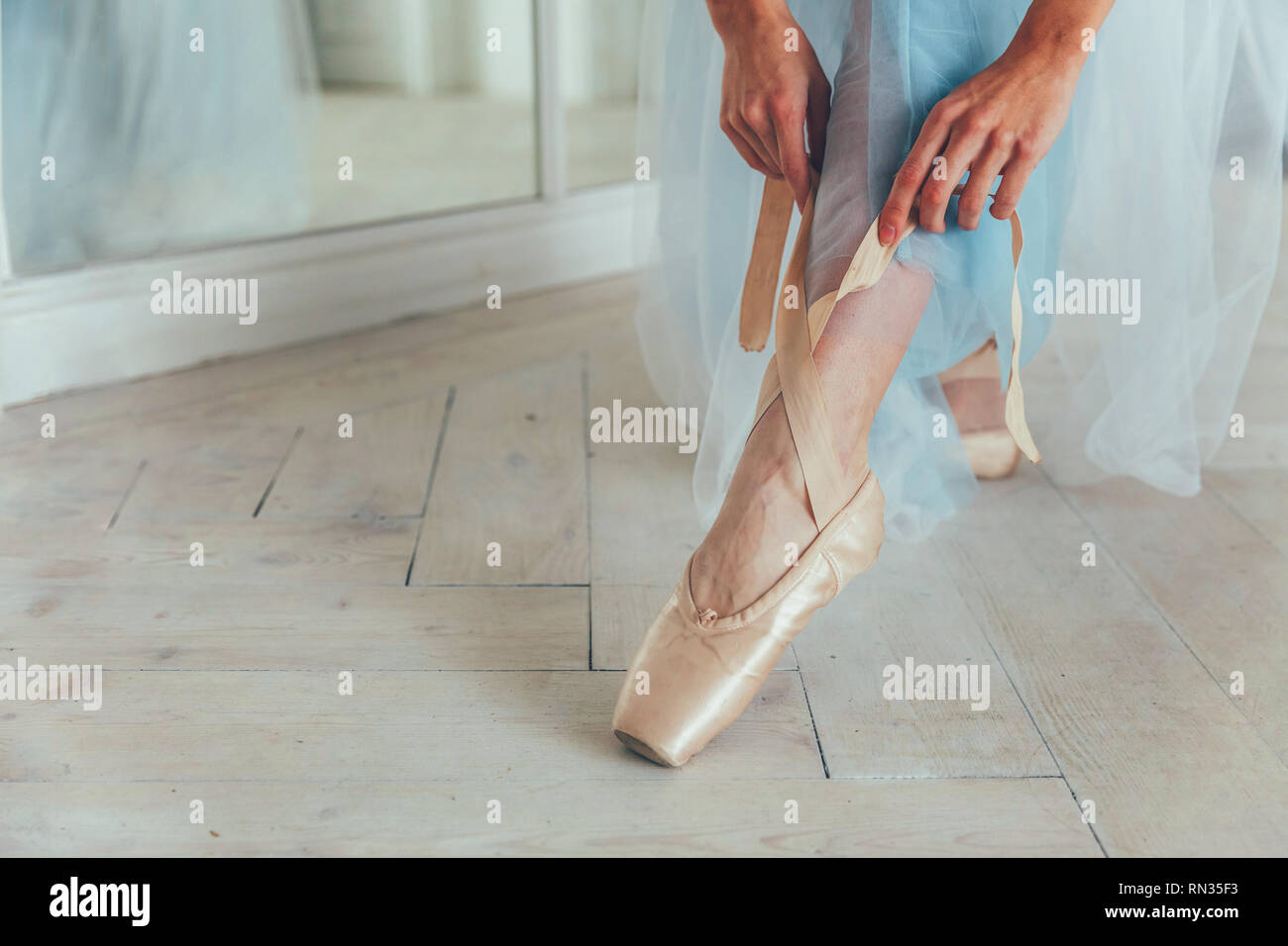 Hands of ballerina in blue tutu skirt puts on pointe shoes on leg in ...