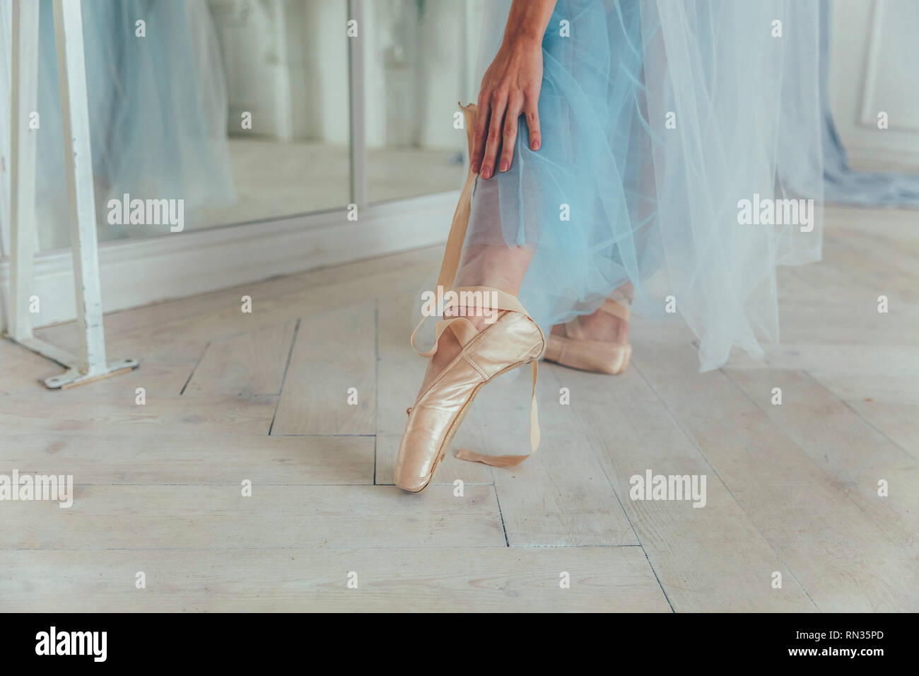 Hands of ballerina in blue tutu skirt puts on pointe shoes on leg in ...