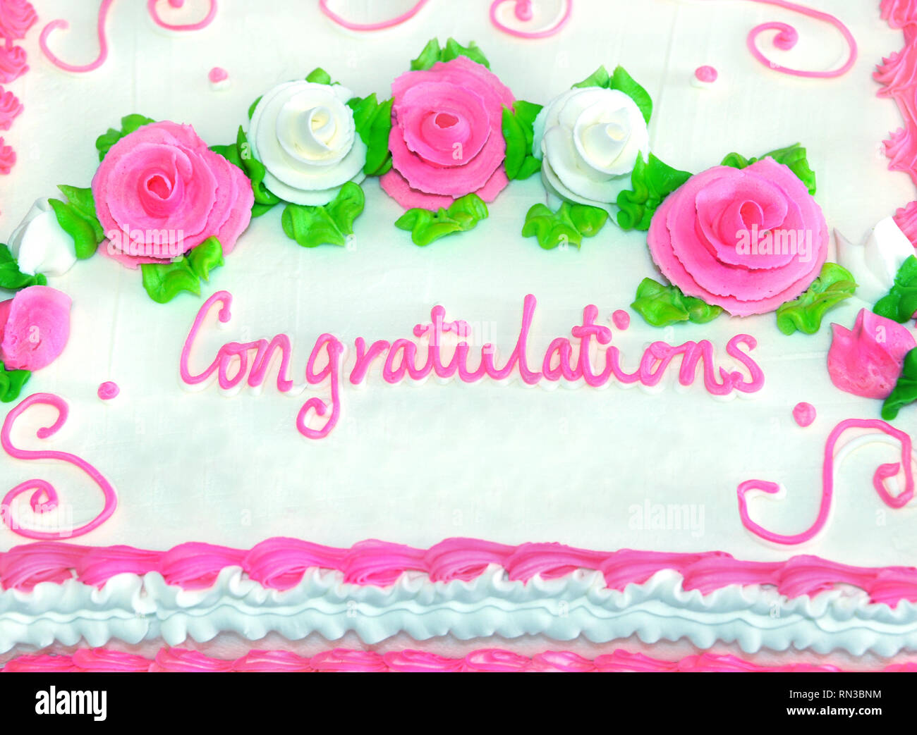 Congratulations in iced writing decorates frosted white cake. Roses in ...