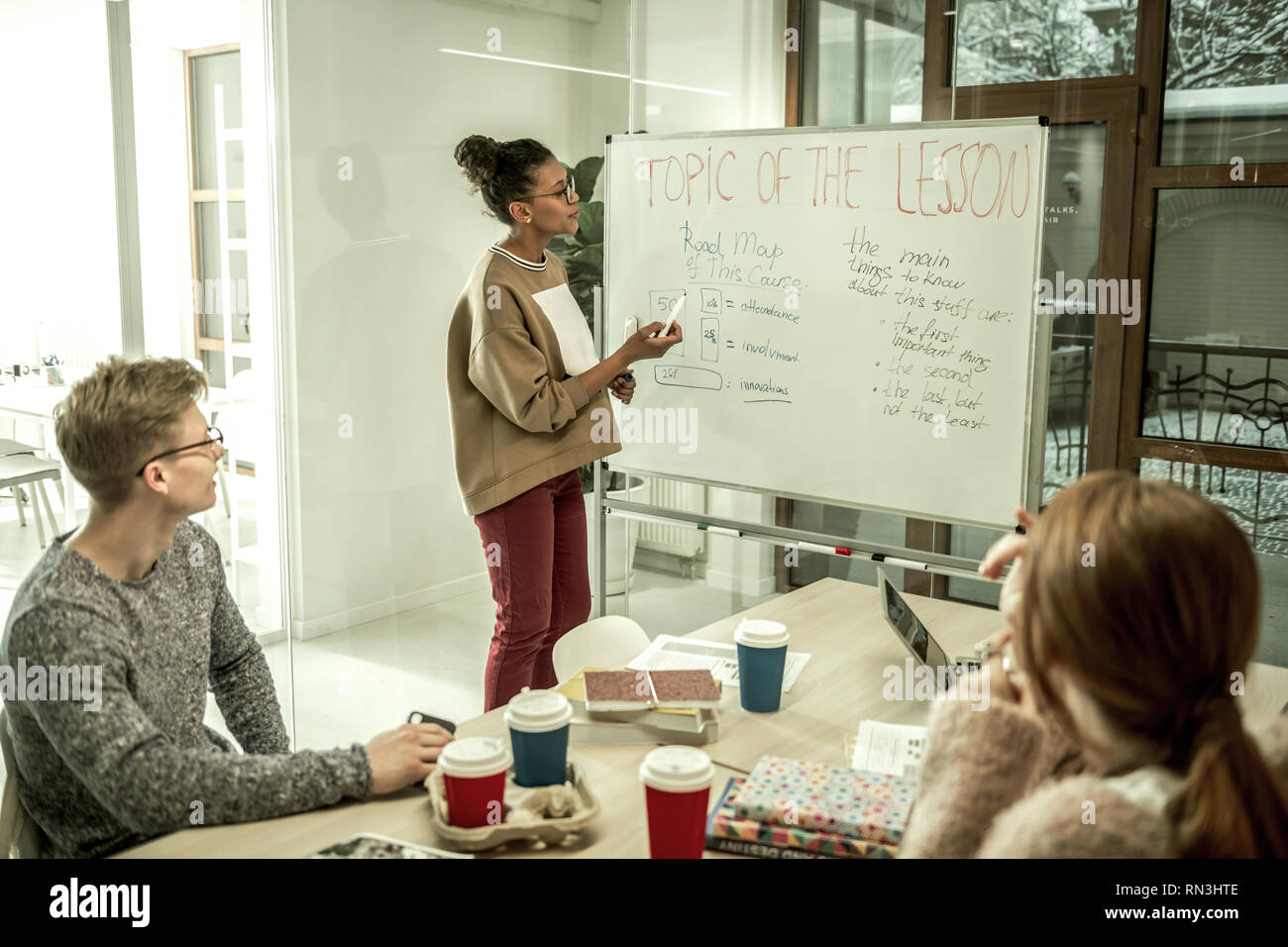Young smart teacher explaining topic of the lesson to her students ...