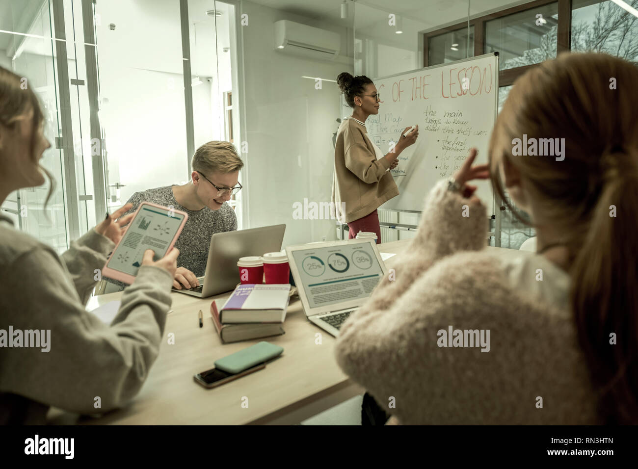 Three modern students using their gadgets during the class Stock Photo ...
