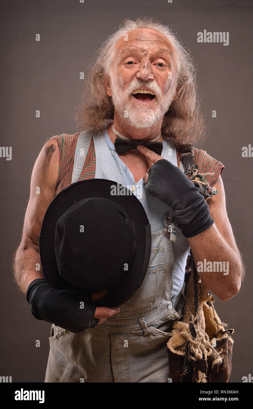 Old homeless but cheerful beggar wearing jeans, black gloves and hat ...