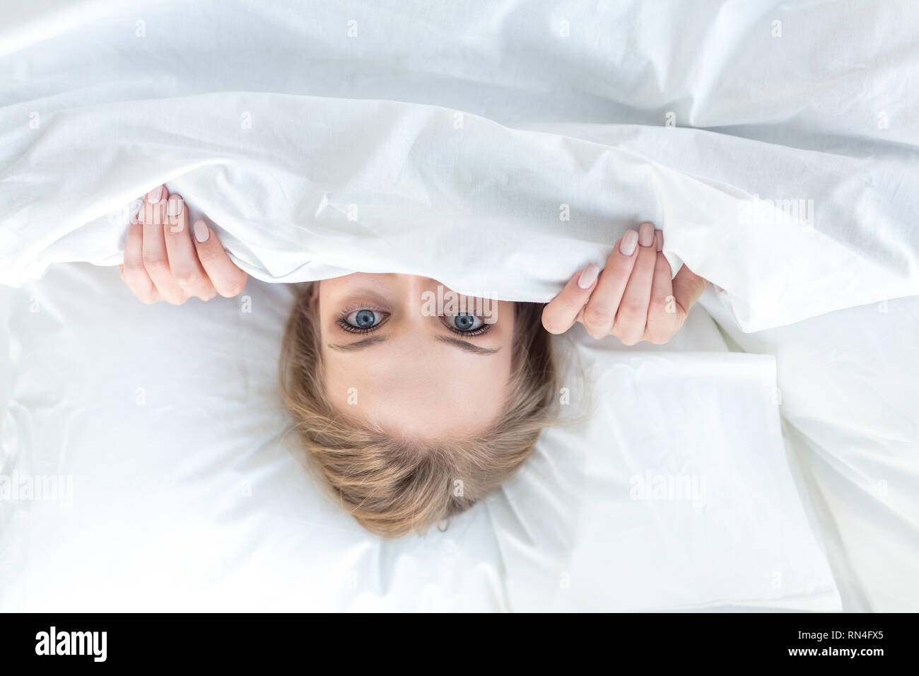 pretty girl hiding under the blanket and looking at the camera, top ...