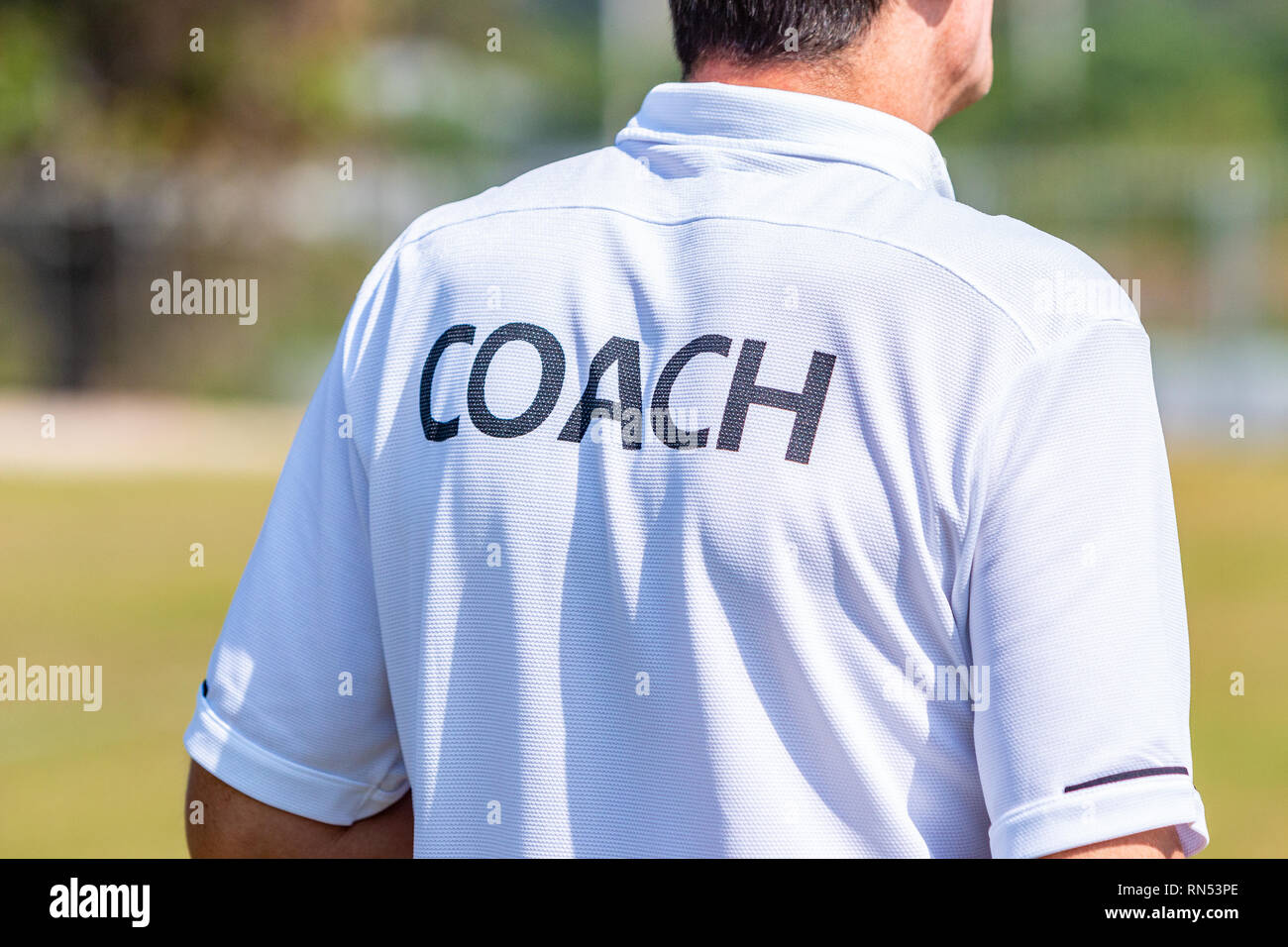 Back view of male sport coach in COACH shirt at an outdoor sport field ...