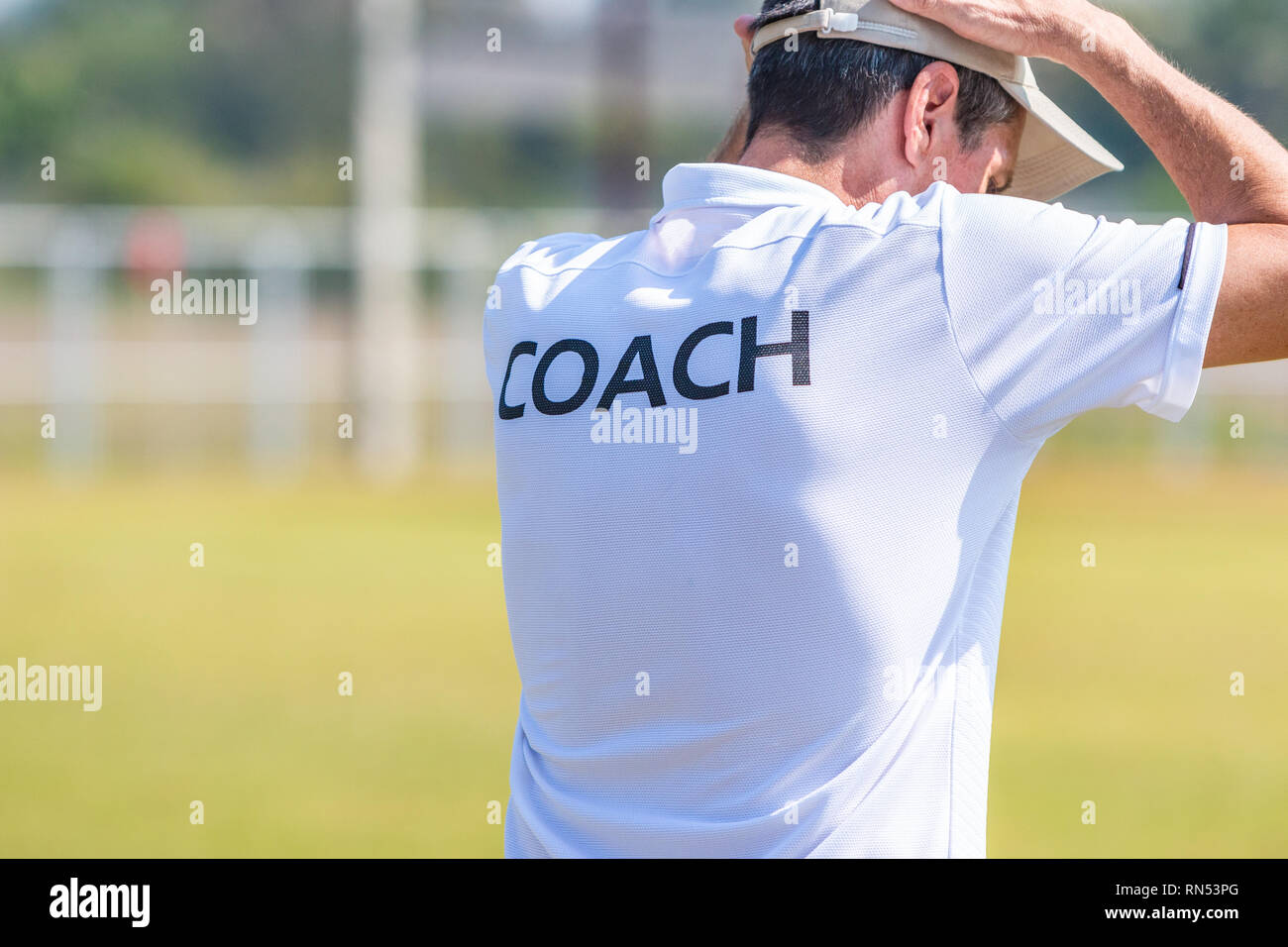 Back view of male sport coach in white COACH shirt at an outdoor sport ...