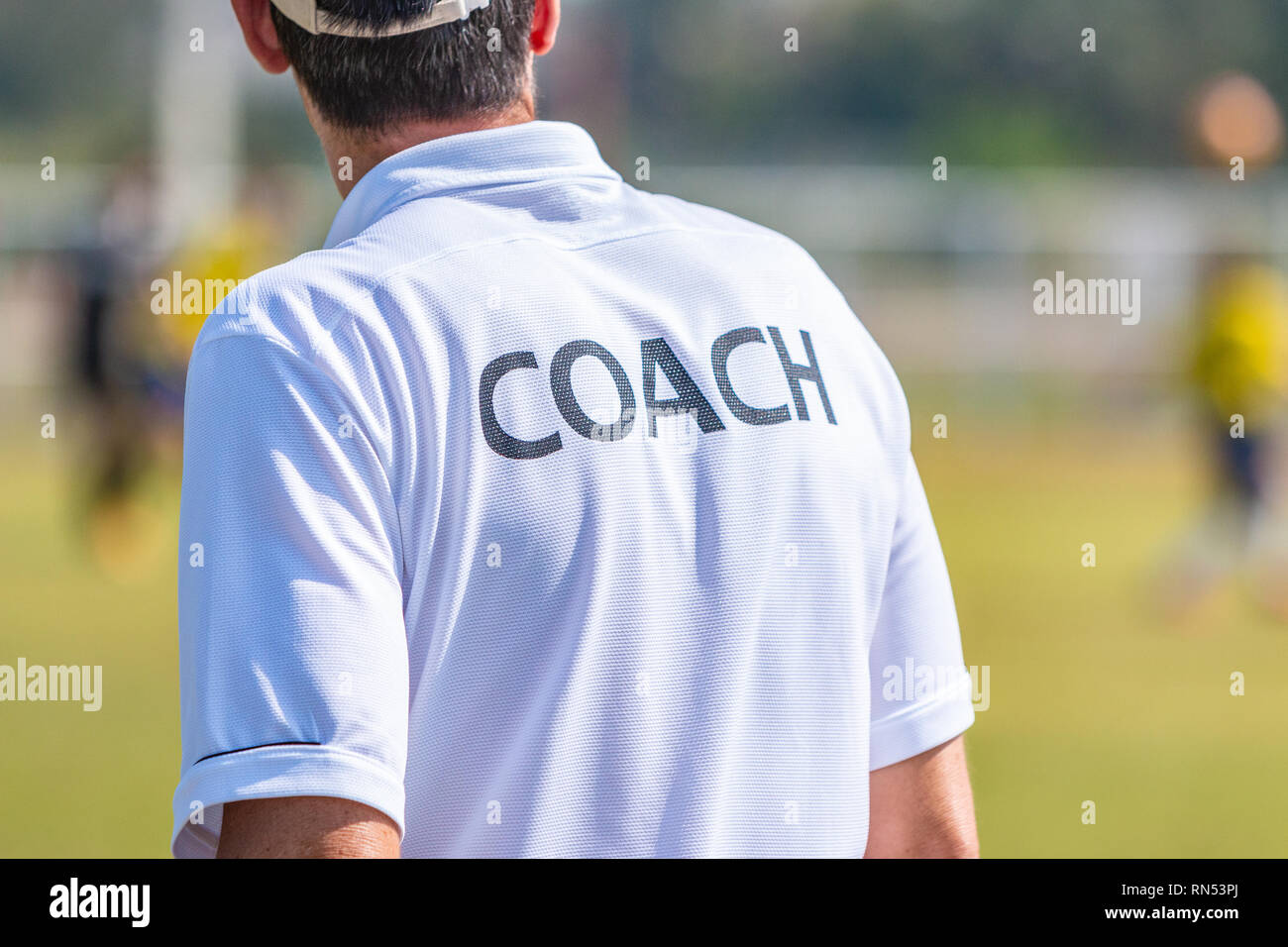 Back view of male sport coach in COACH shirt at an outdoor sport field ...