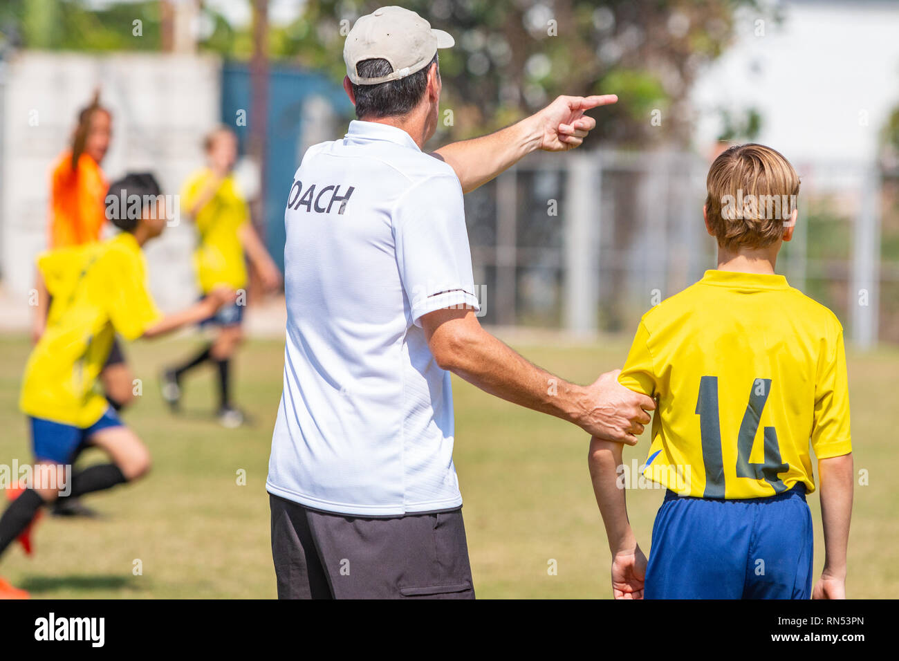 Back of male football coach wearing white COACH shirt at an outdoor ...