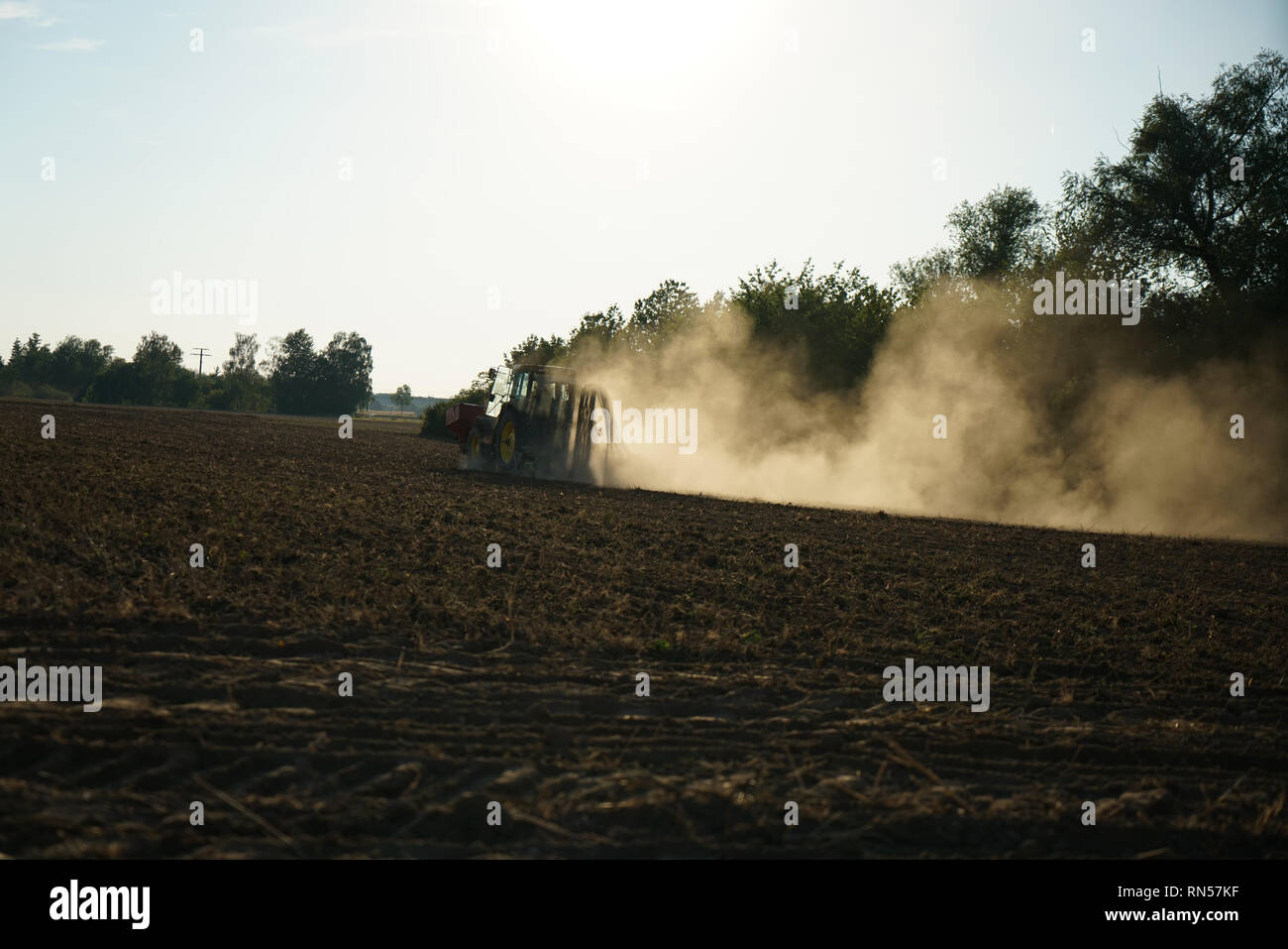 Just before sunset, a farmer was still working on a dusty field Stock ...