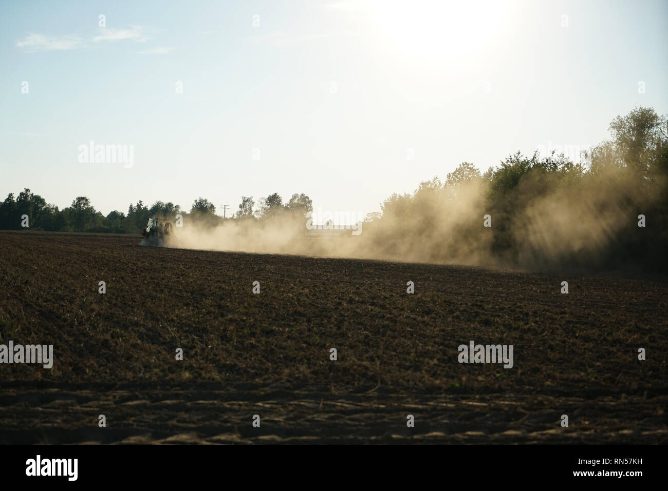 Just before sunset, a farmer was still working on a dusty field Stock ...