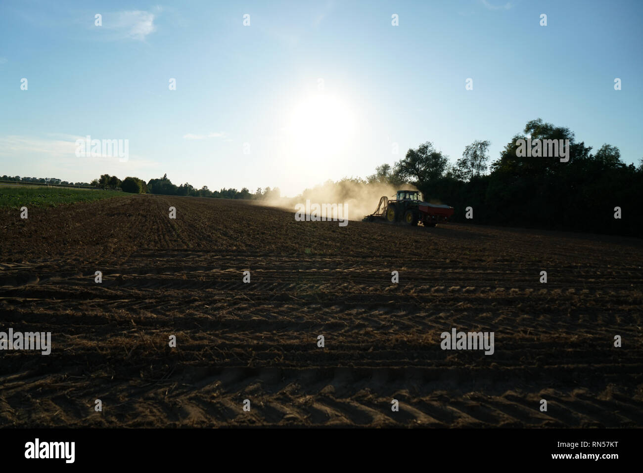 Just before sunset, a farmer was still working on a dusty field Stock ...