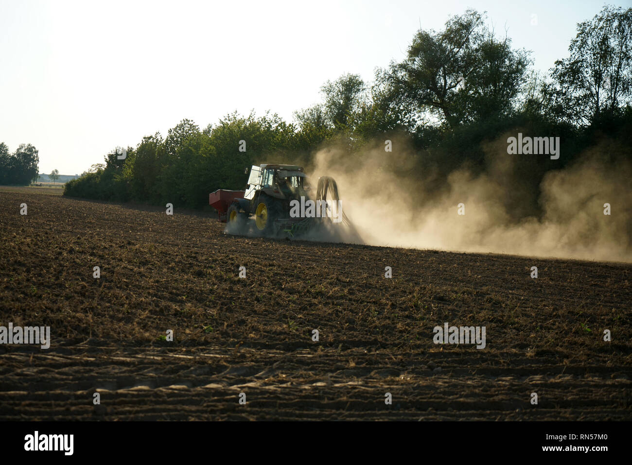 Just before sunset, a farmer was still working on a dusty field Stock ...