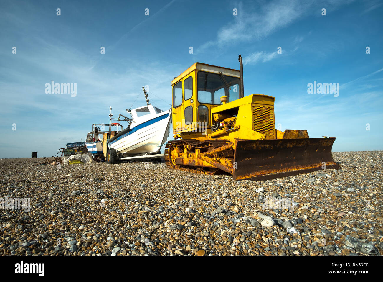 Old yellow bulldozer towing a small fishing boat on a pebble beach ...