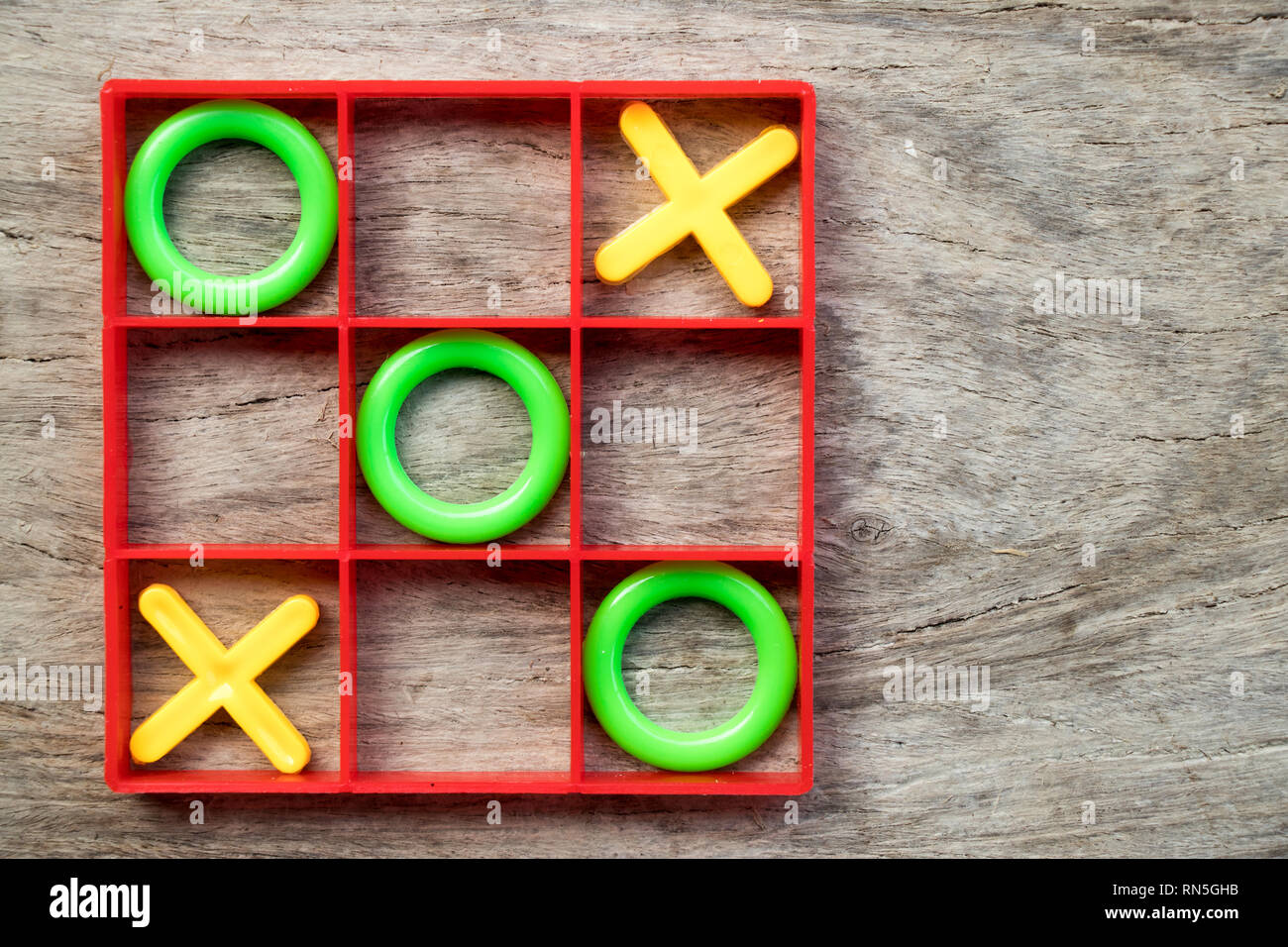 Tic-tac-toe board game with green O and yellow X in red frame on wood ...