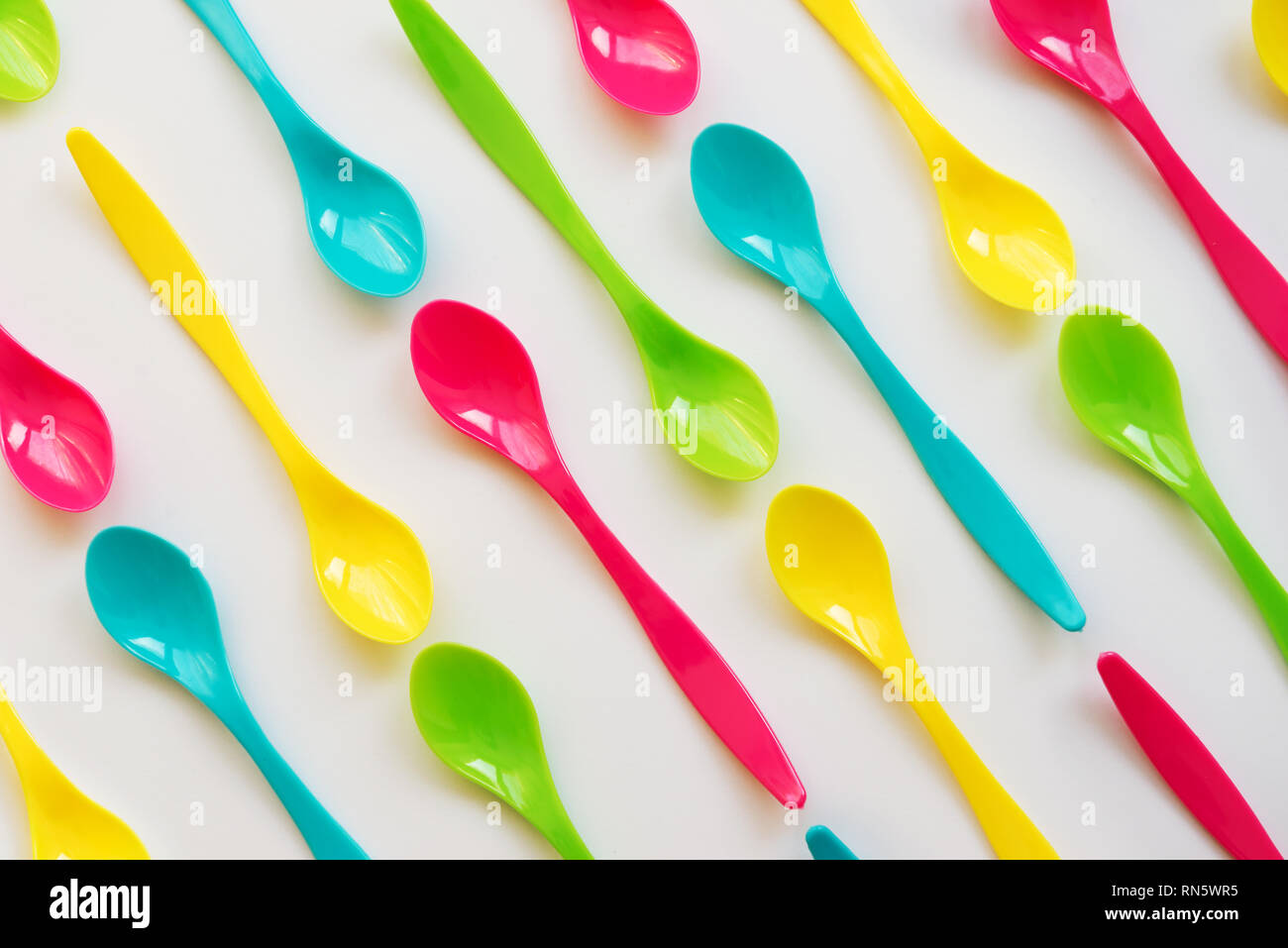 Many colorful plastic spoons on white background, top view. Concept of ...
