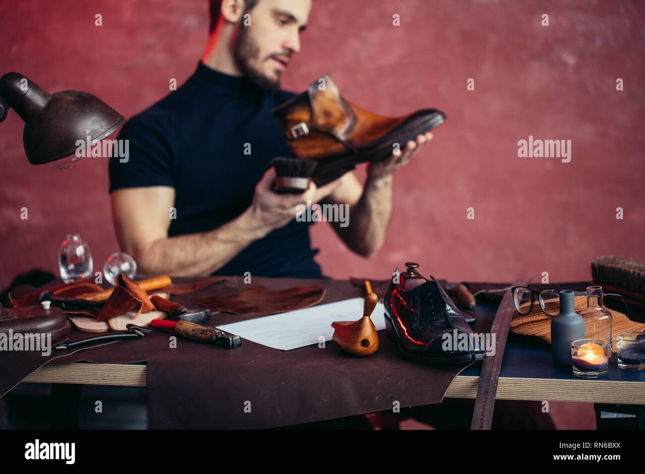 focus on polished leather shoe lying on the desk, handsome shoemaker on ...