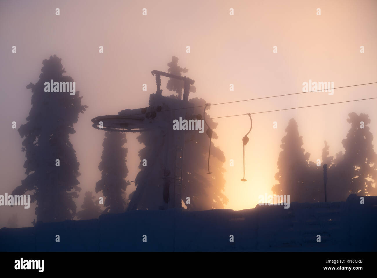 Silhouette of ski lift and trees at winter against golden sunset with ...