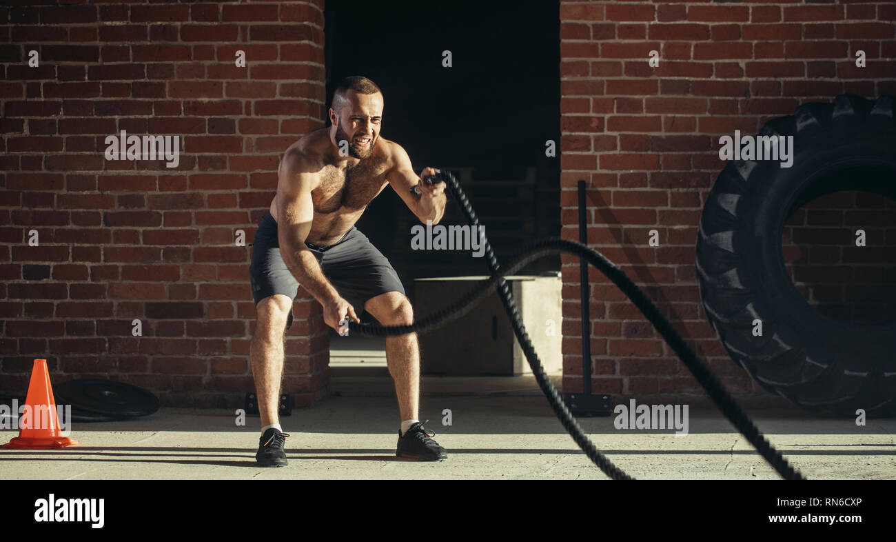 Athletic young man with battle rope doing exercise in functional ...
