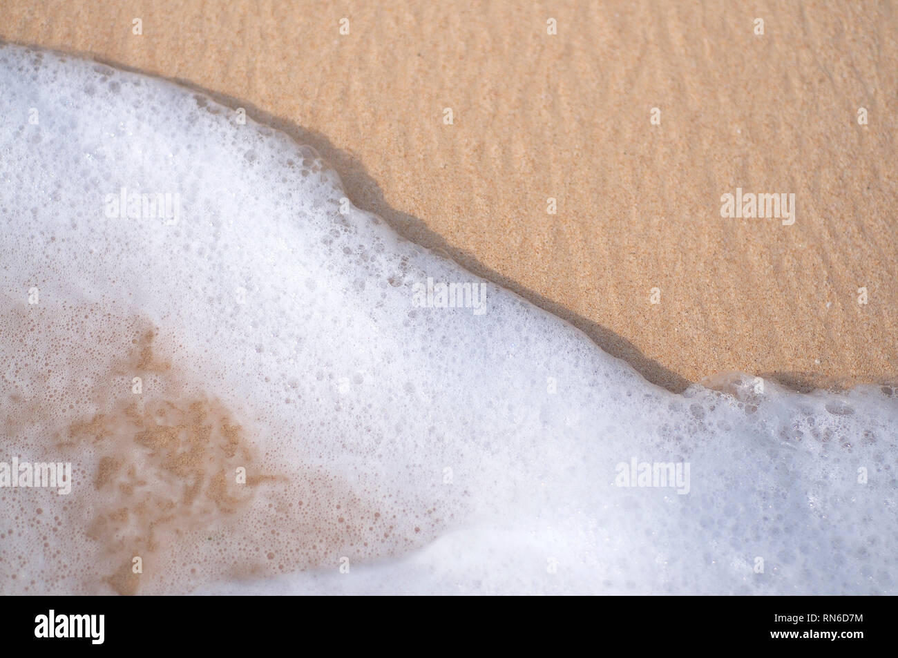 Close up picture of sand at the beach while the wave's foam is coming ...