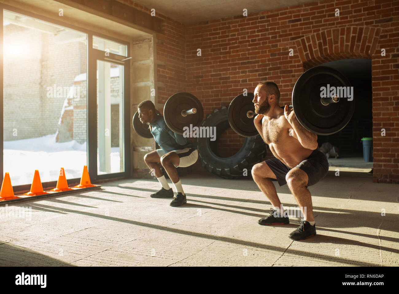 African fitness coach teaches his caucasian male client to lift heavy ...