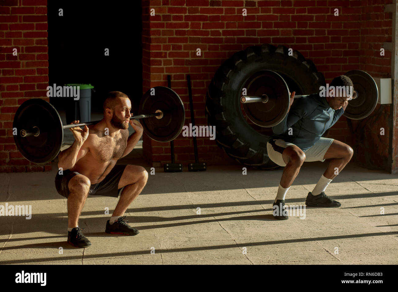 African fitness coach teaches his caucasian male client to lift heavy ...