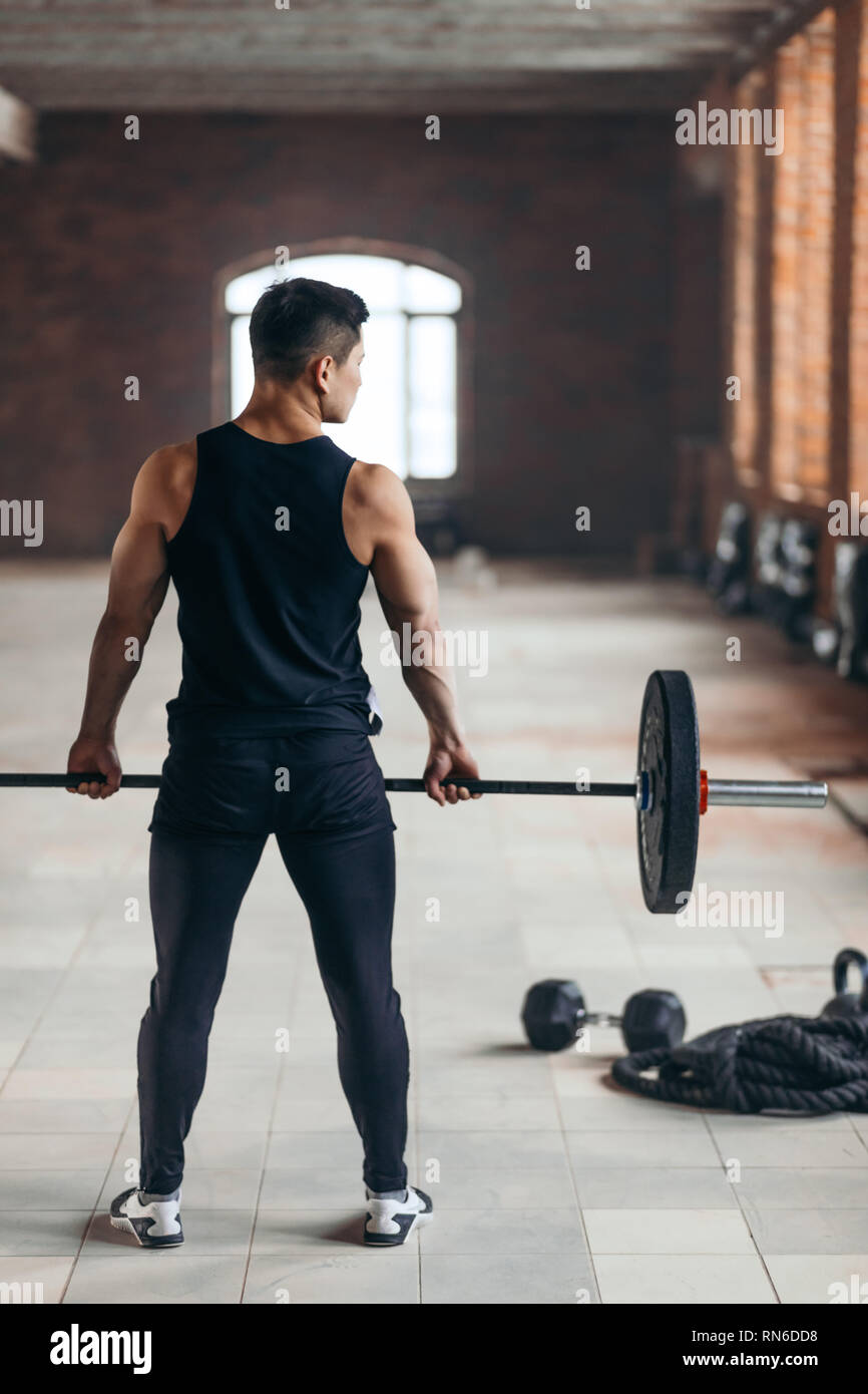 athlete lifting loaded barbell off the ground. full length back view ...