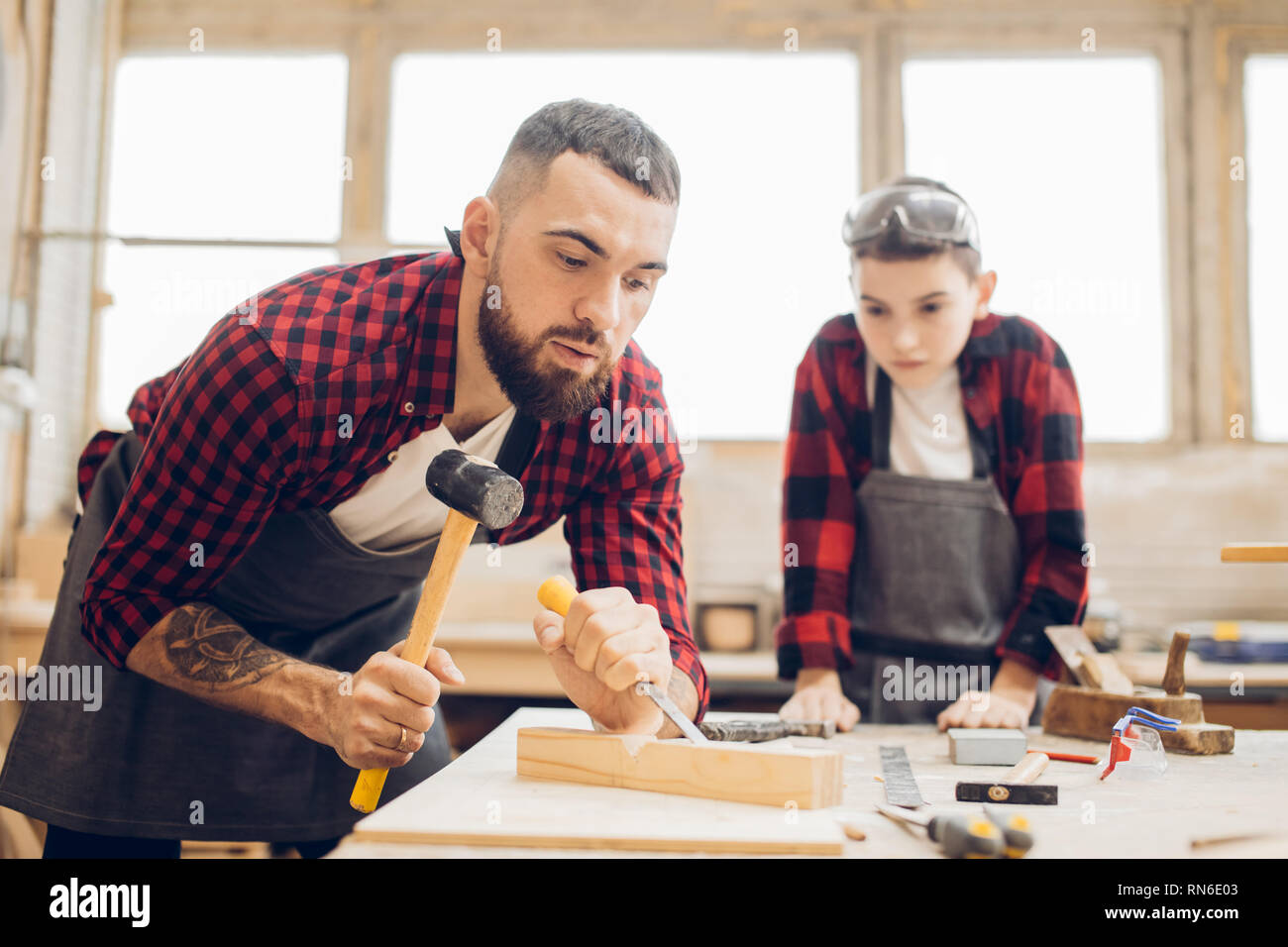 Bearded jointer man in safety glasses and an apron works with chisel in ...