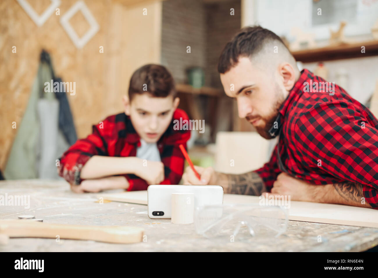 Focused craftsman and his little follower boy are measuring wood using ...