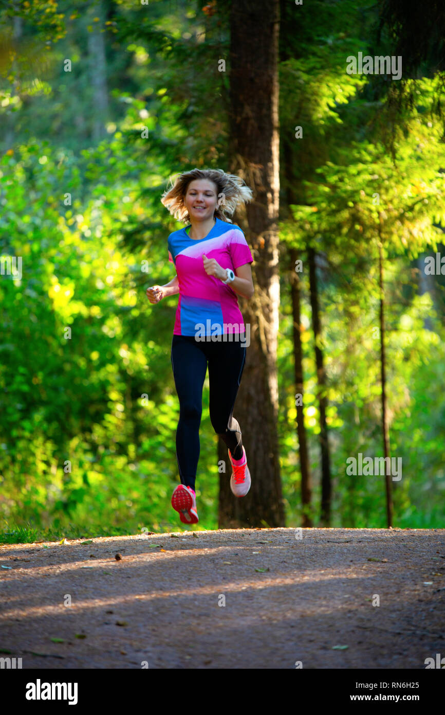 Blonde athlete woman running through park among trees on summer Stock ...