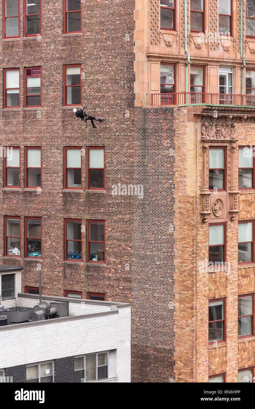 Industrial engineer rappelling down the side of a building on a ...