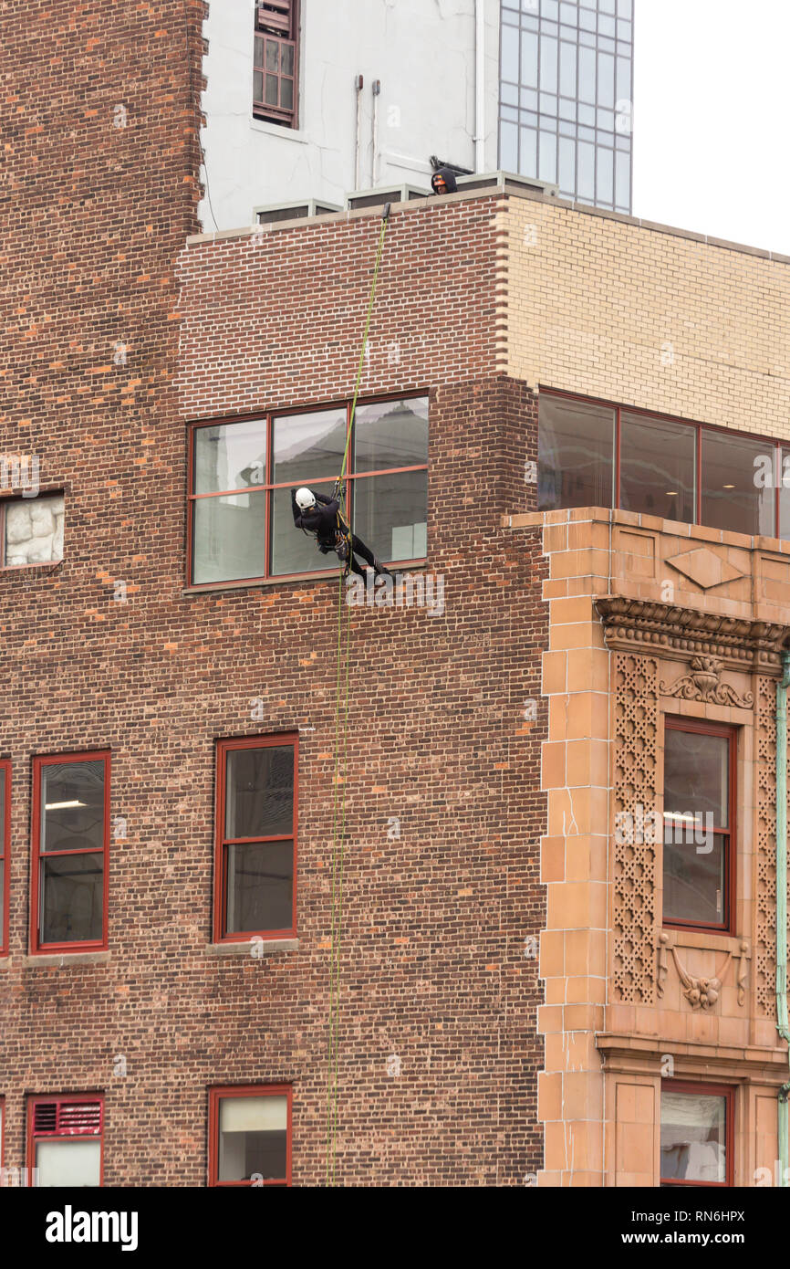 Industrial engineer rappelling down the side of a building on a ...