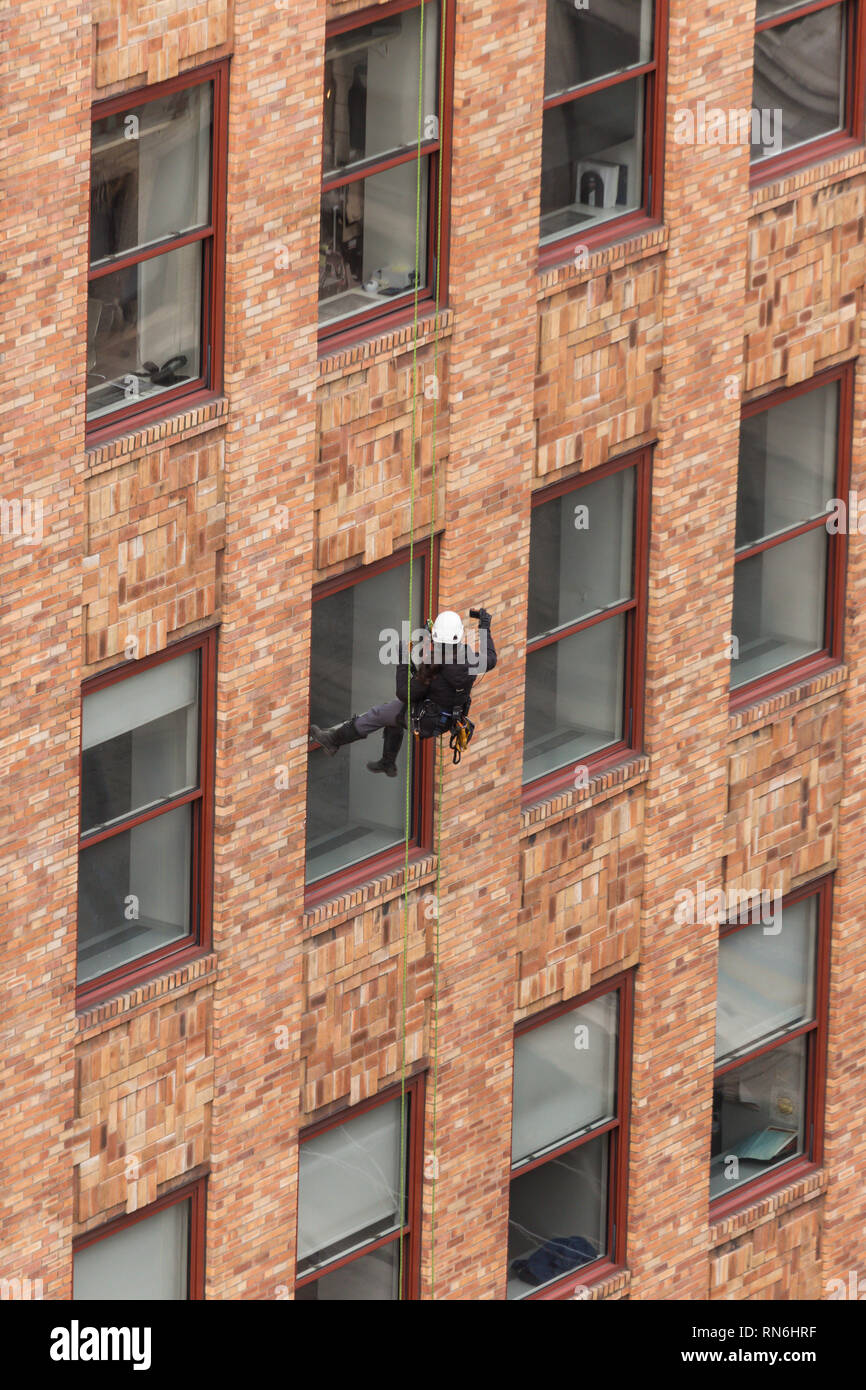 Industrial engineer rappelling down the side of a building on a ...