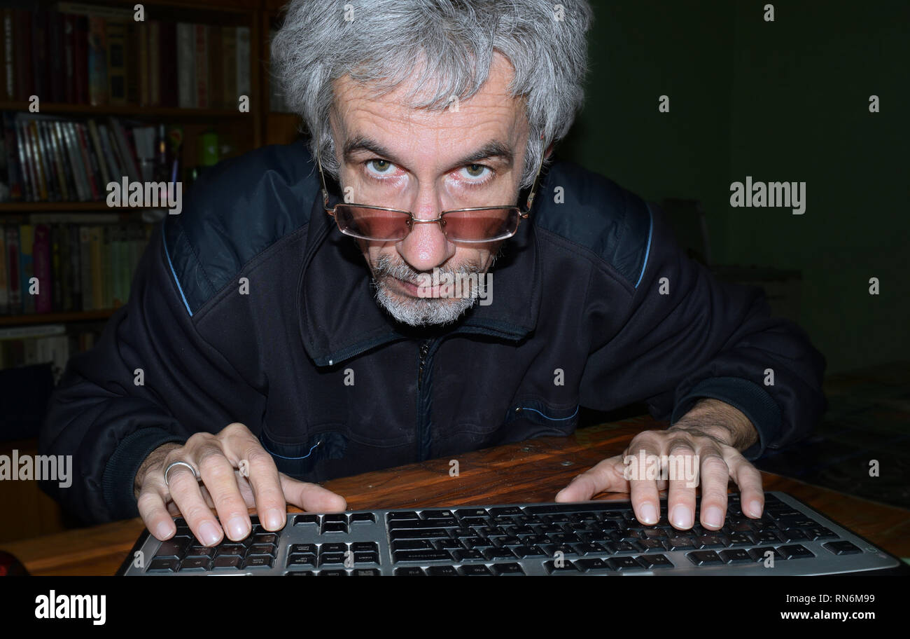portrait of a gray-haired man with a keyboard in front of computer ...