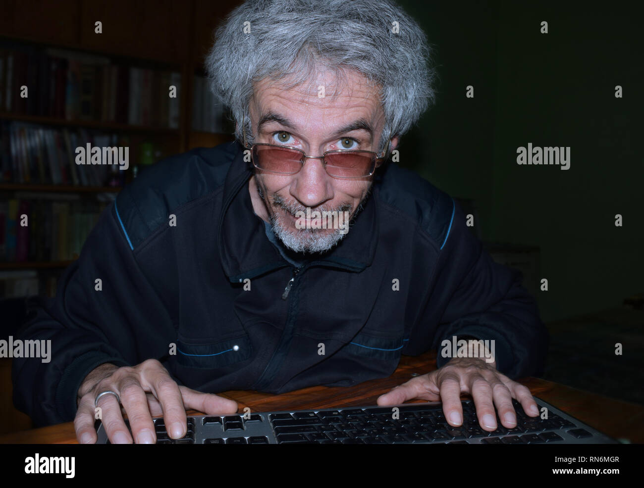 portrait of a gray-haired man with a keyboard in front of computer ...