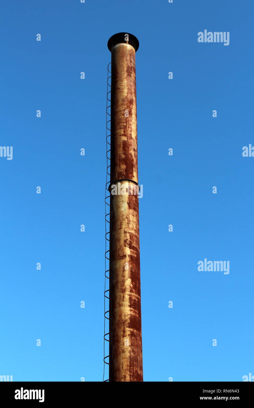 Tall narrow completely rusted old industrial chimney with side steps ...