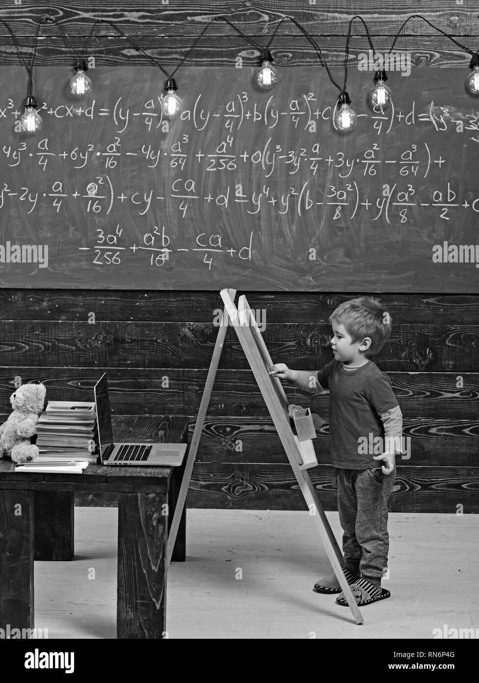 Little boy writing on chalkboard. Side view kid in front of green board ...