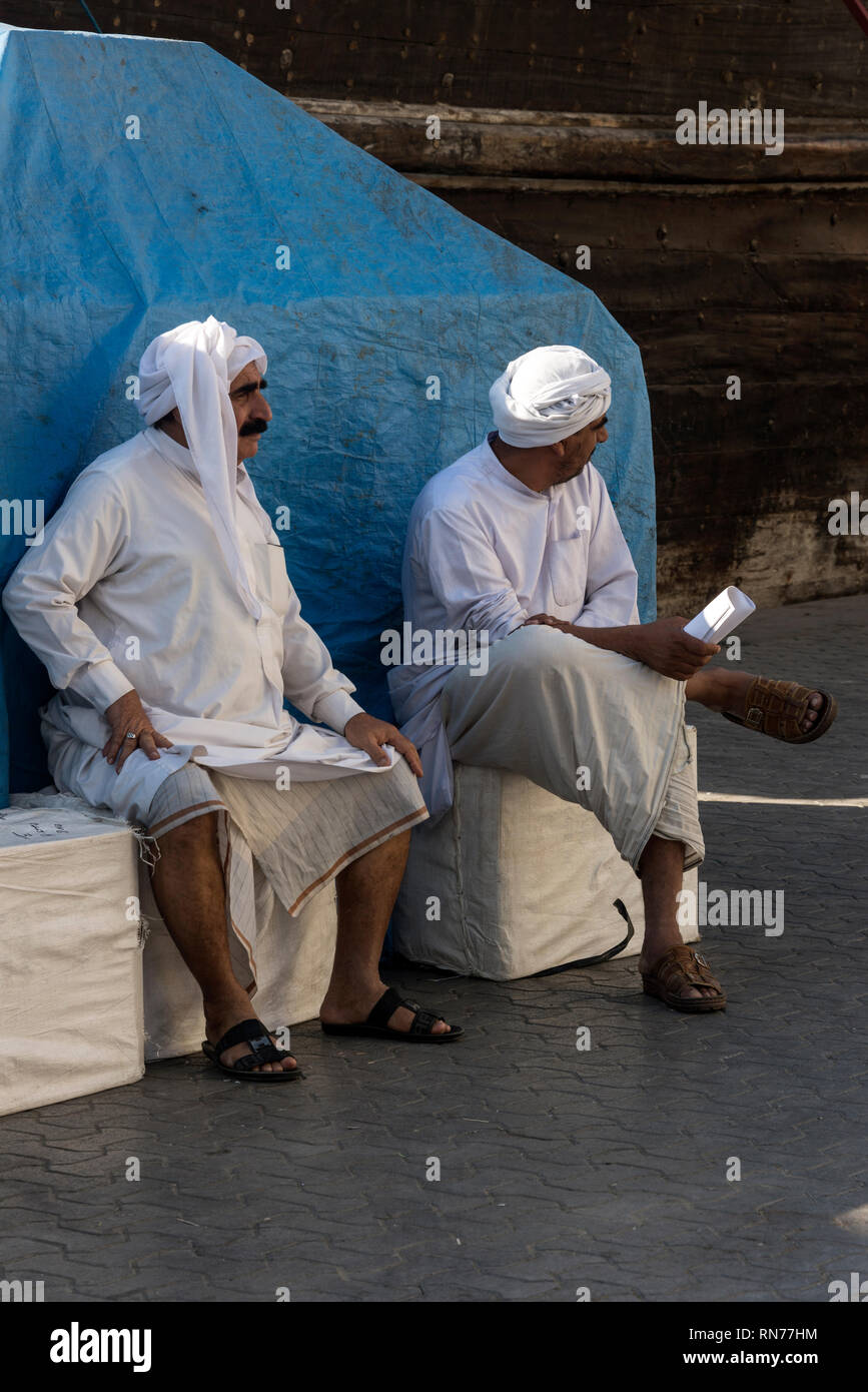 Two Asian dock workers taking a rest on the quay on Dubai Creek in ...