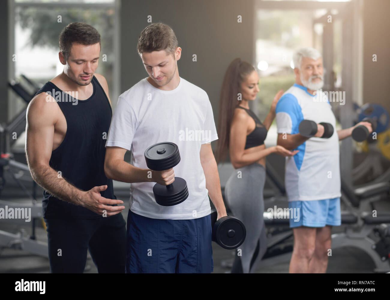 Modern gym with professional, muscular trainers. Coach helping man to ...