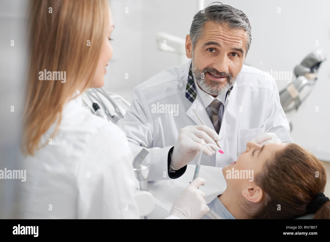 Woman with opened mouth lying in dentist chair. Handsome bearded ...