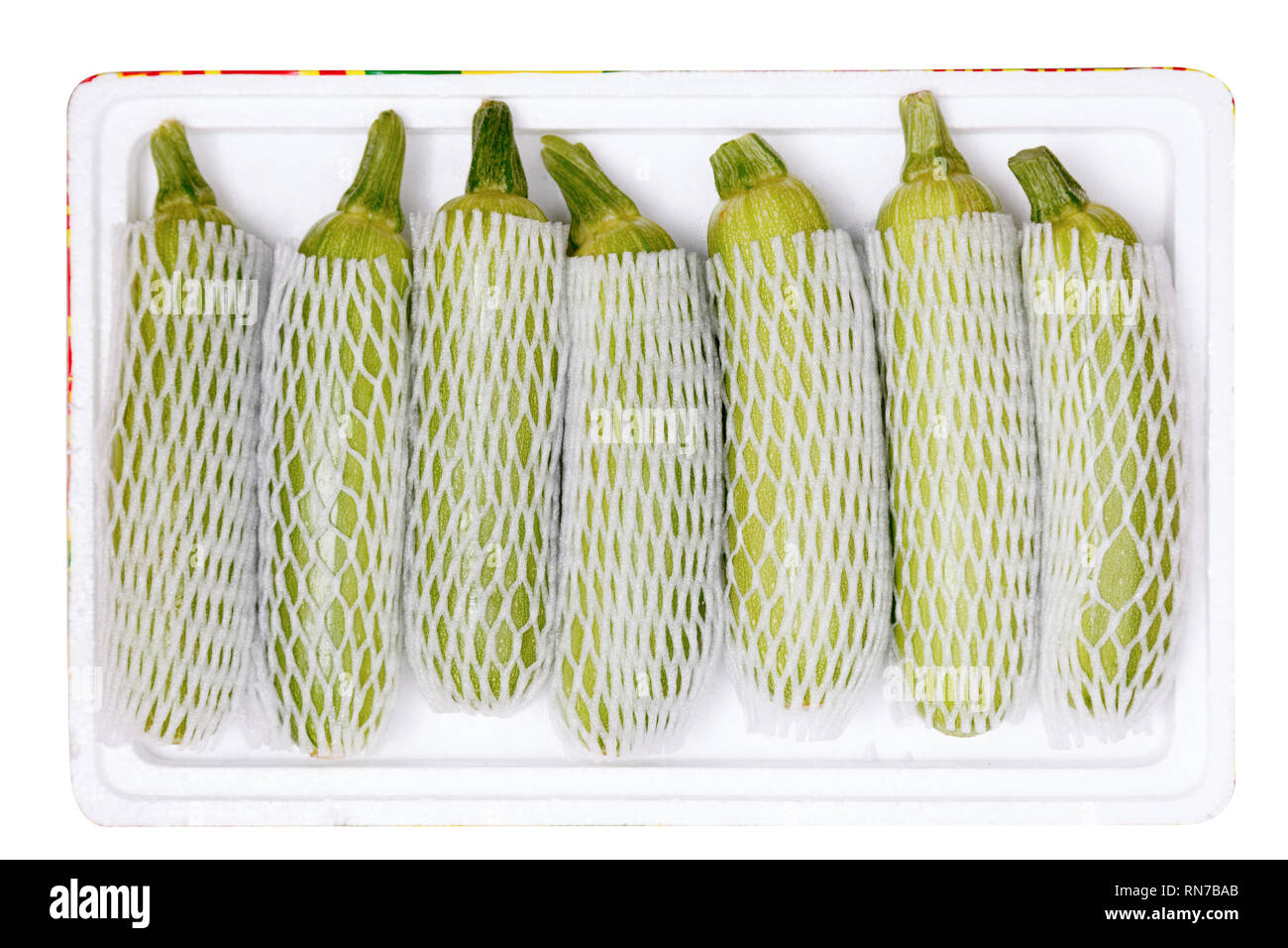 Closeup fresh green zucchini in grid package are on white tray isolated ...