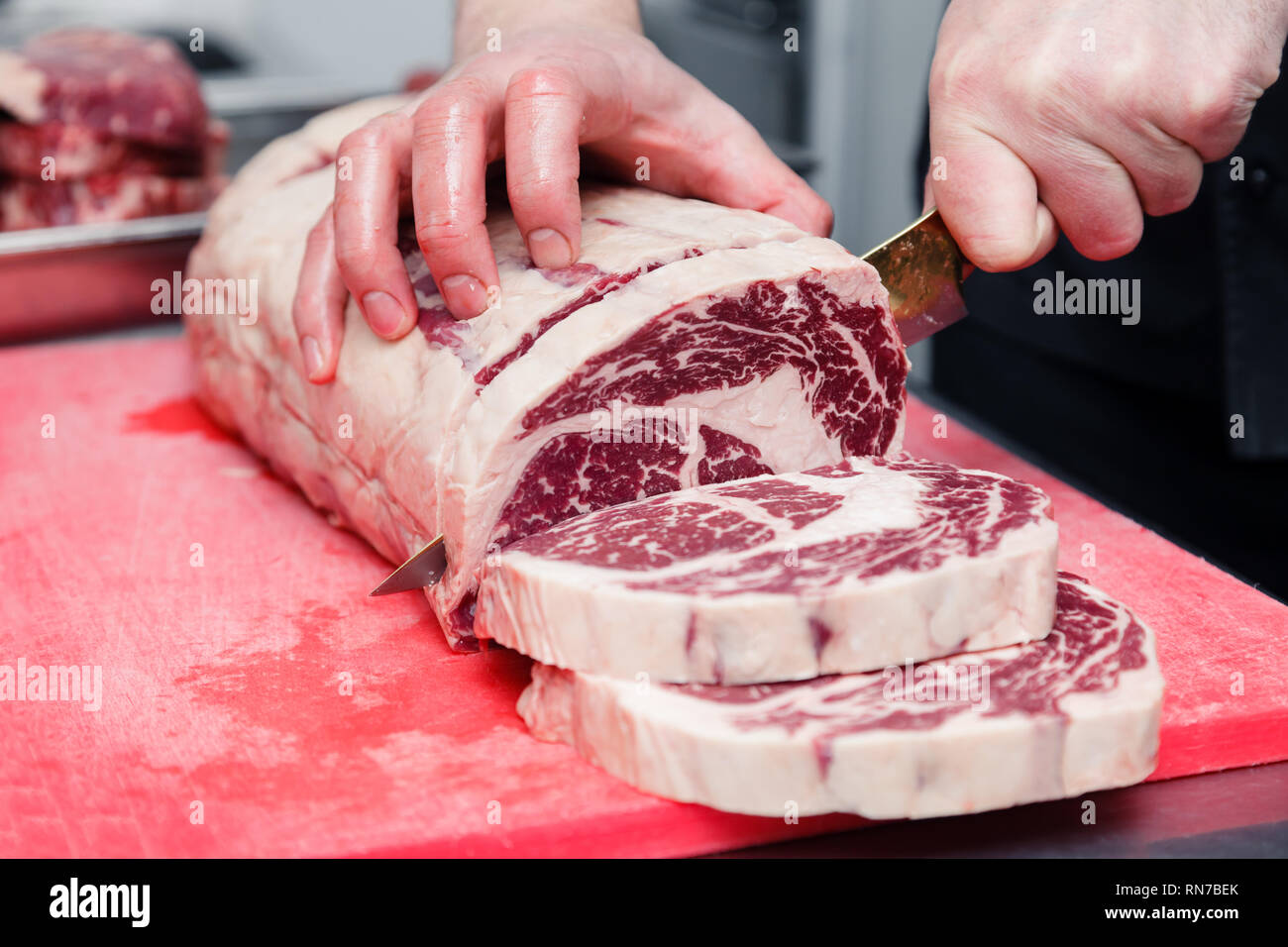 Closeup macro cook's hand cut ribeye marbled beef steak with knife on ...