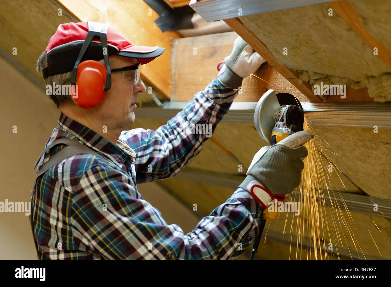 Man fixing metal frame using angle grinder on attic ceiling covered ...