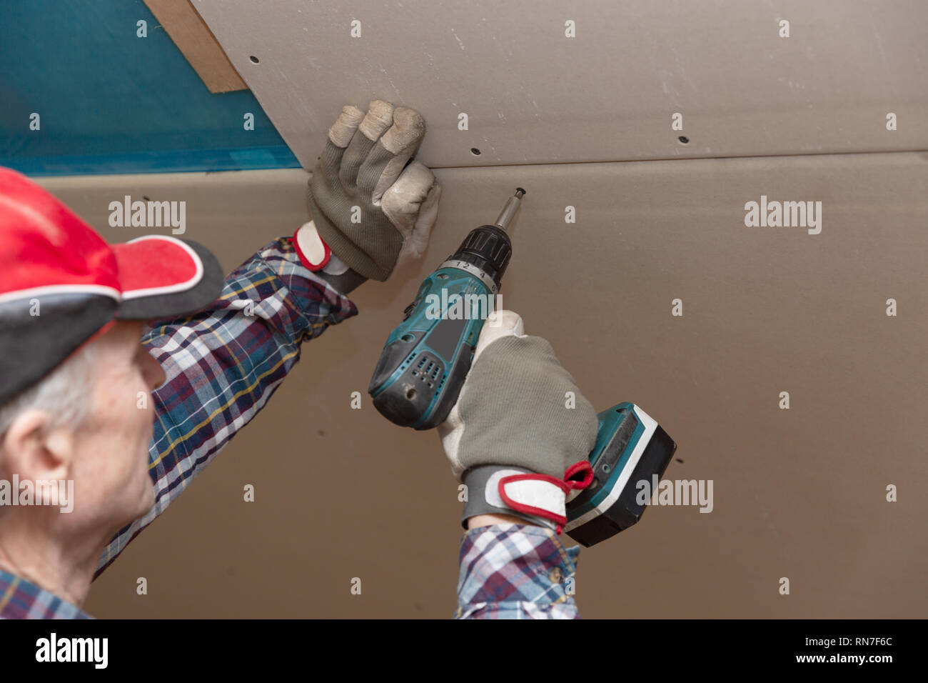 Drywall construction, attic renovation. Man fixing drywall suspended ...